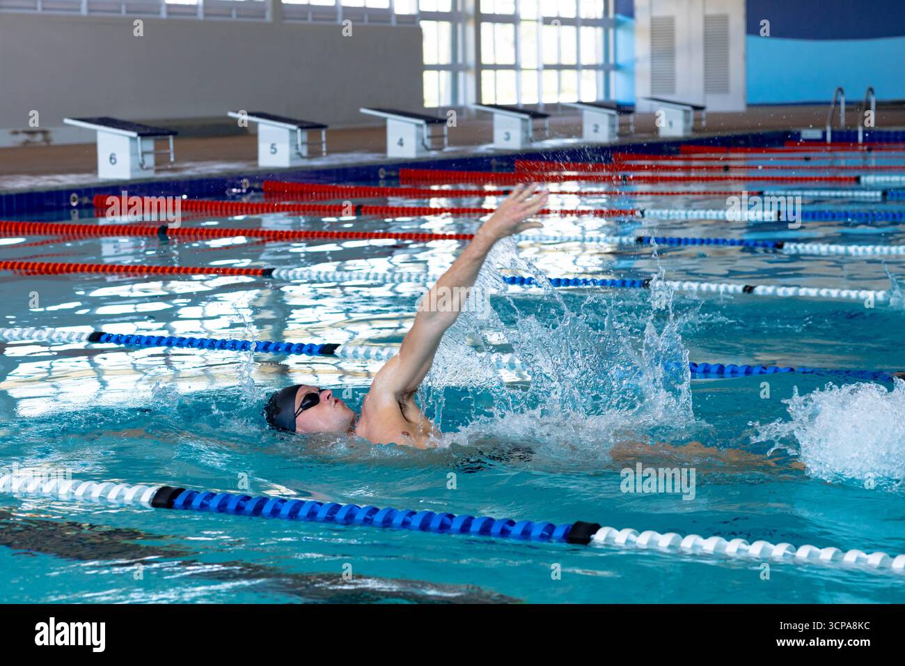 Male swimmer performing backstroke in pool with goggles, black swim cap ...