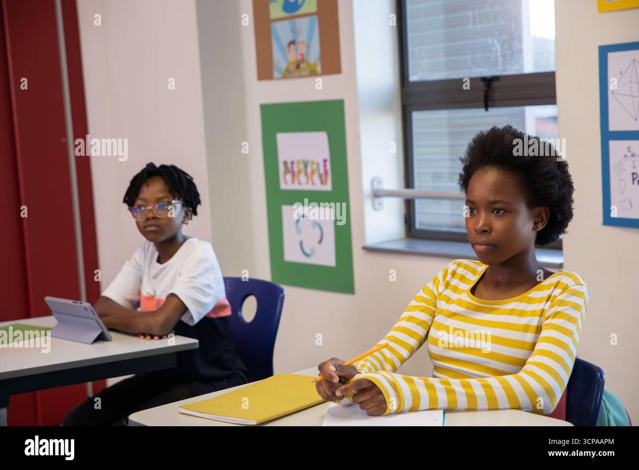 African american classmates sitting at desks tapping tablet, writing ...