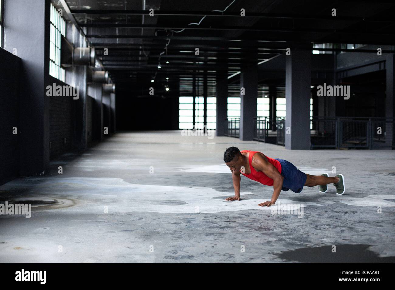 African American man performing push-up on warehouse floor by columns ...