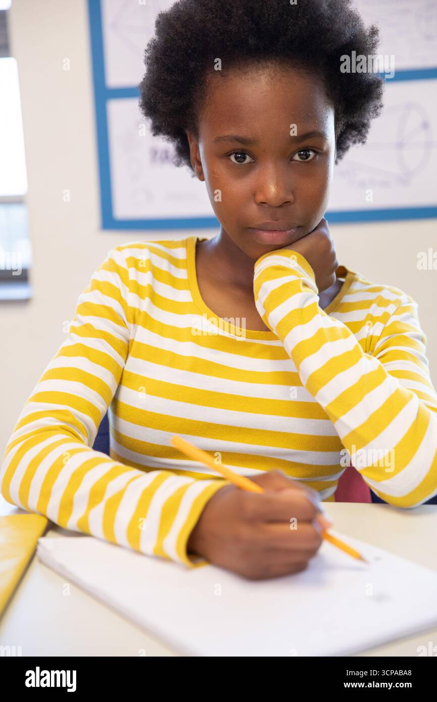 African american girl writing on paper at school desk with pencil ...