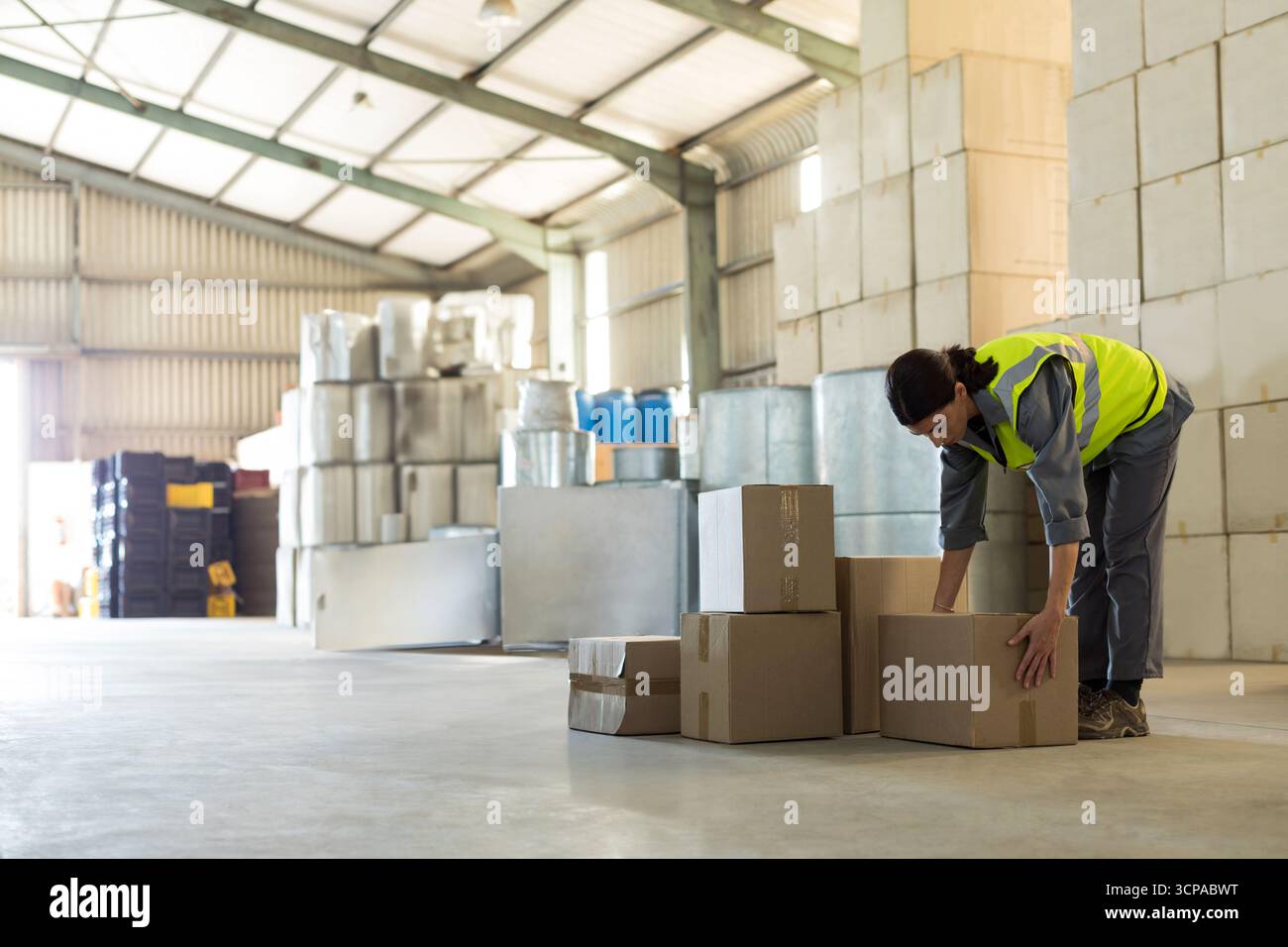 Female warehouse worker stacking boxes on warehouse floor with barrels ...