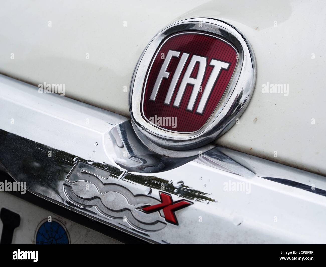 A close-up of a white car's front with two emblems. The main one is the ...