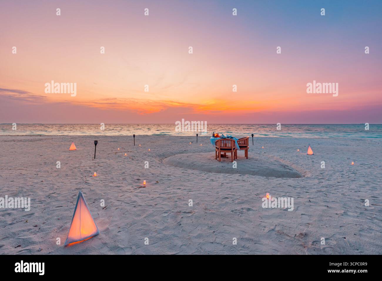 Fantastic sunset beach dinner with romantic candles and a colorful sky ...