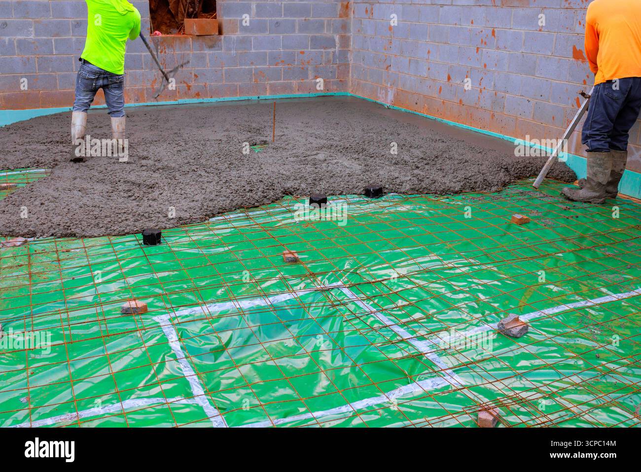 Workers pour wet concrete onto slab covered with protective sheet ...