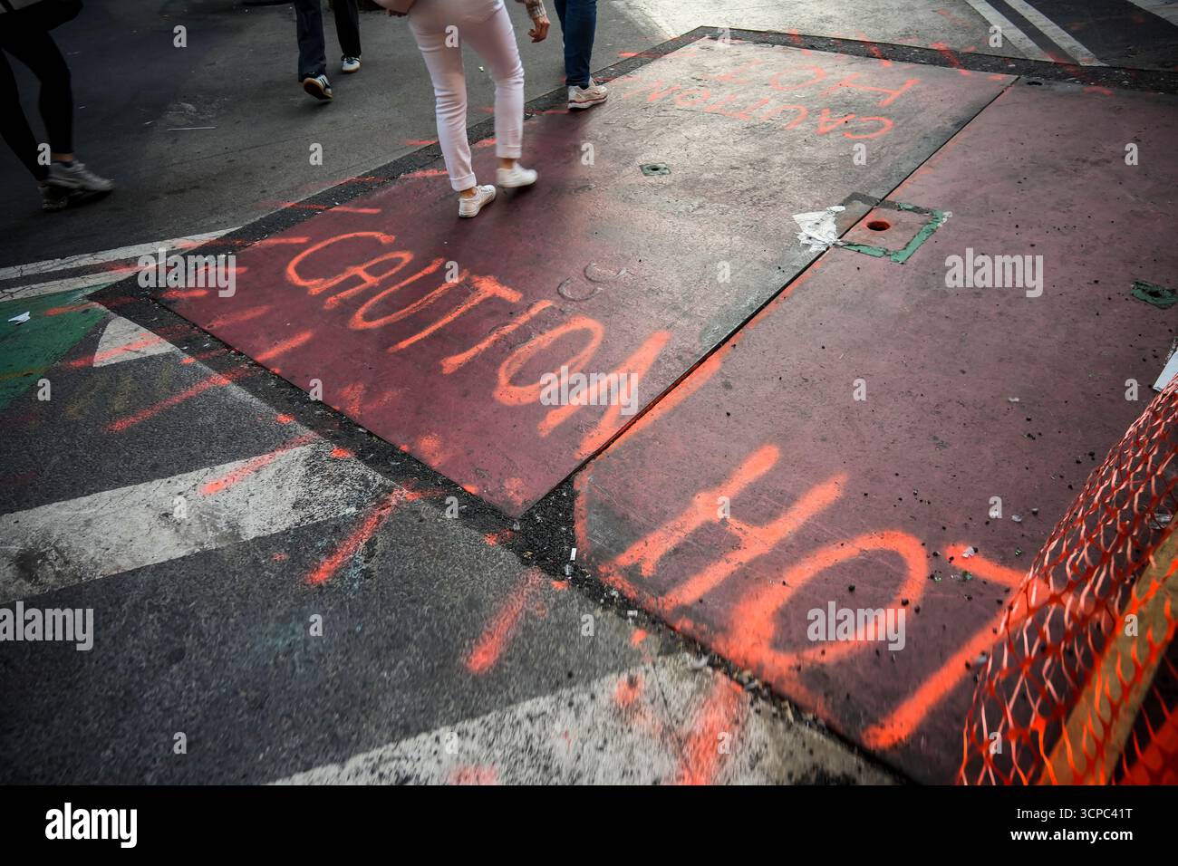Pedestrians walk over a protective plate in the road marked hot during ...