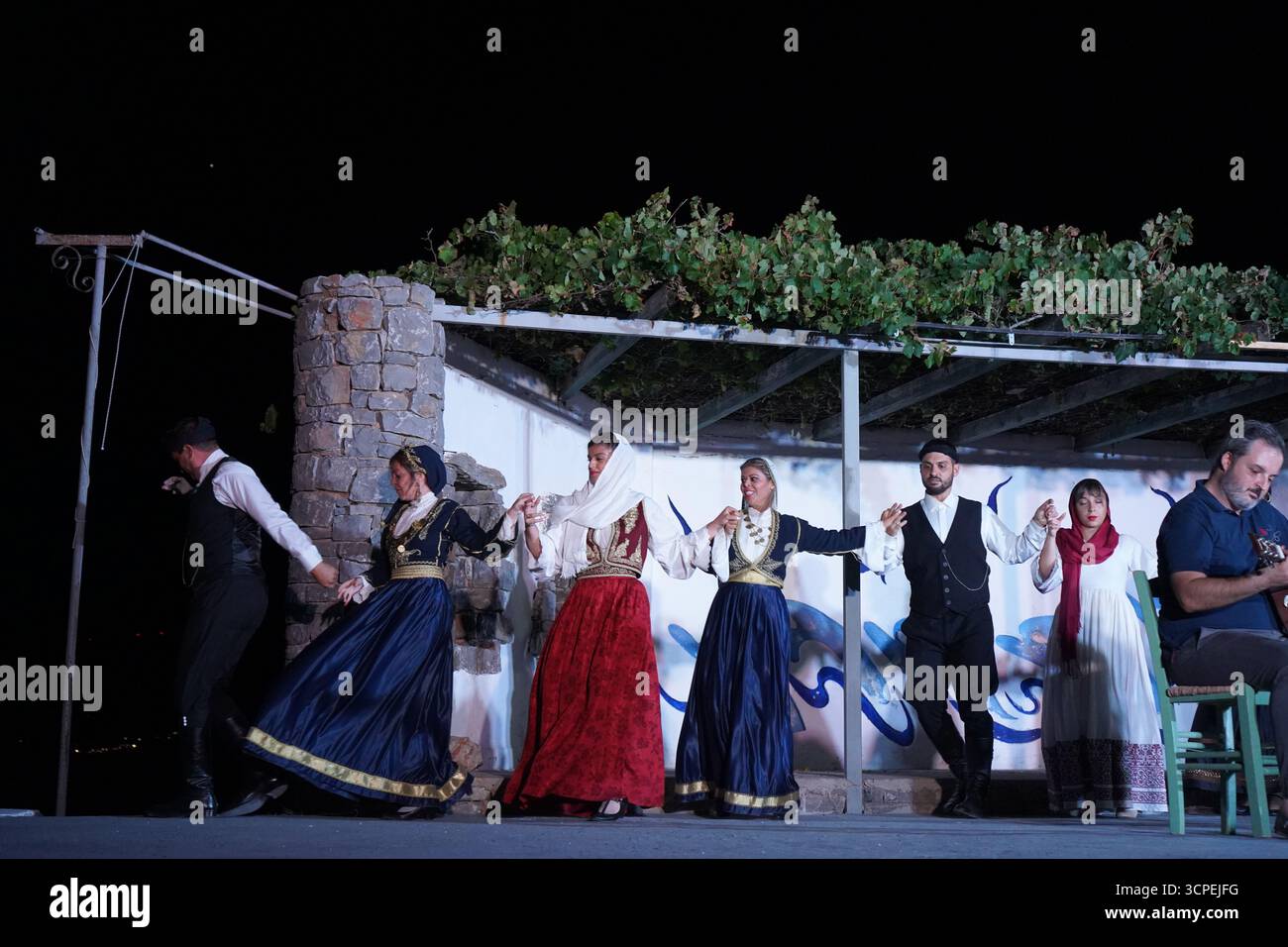 A vibrant scene of men and women in traditional Cretan attire dancing ...