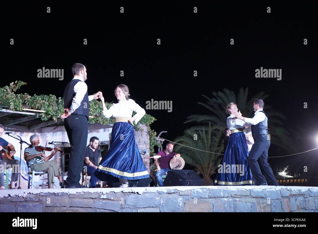 Men and women in traditional Cretan costumes dance to the rhythm of ...