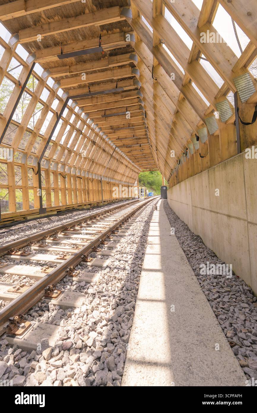 Wooden tunnel structure over railway tracks, bright sunlight floods the ...