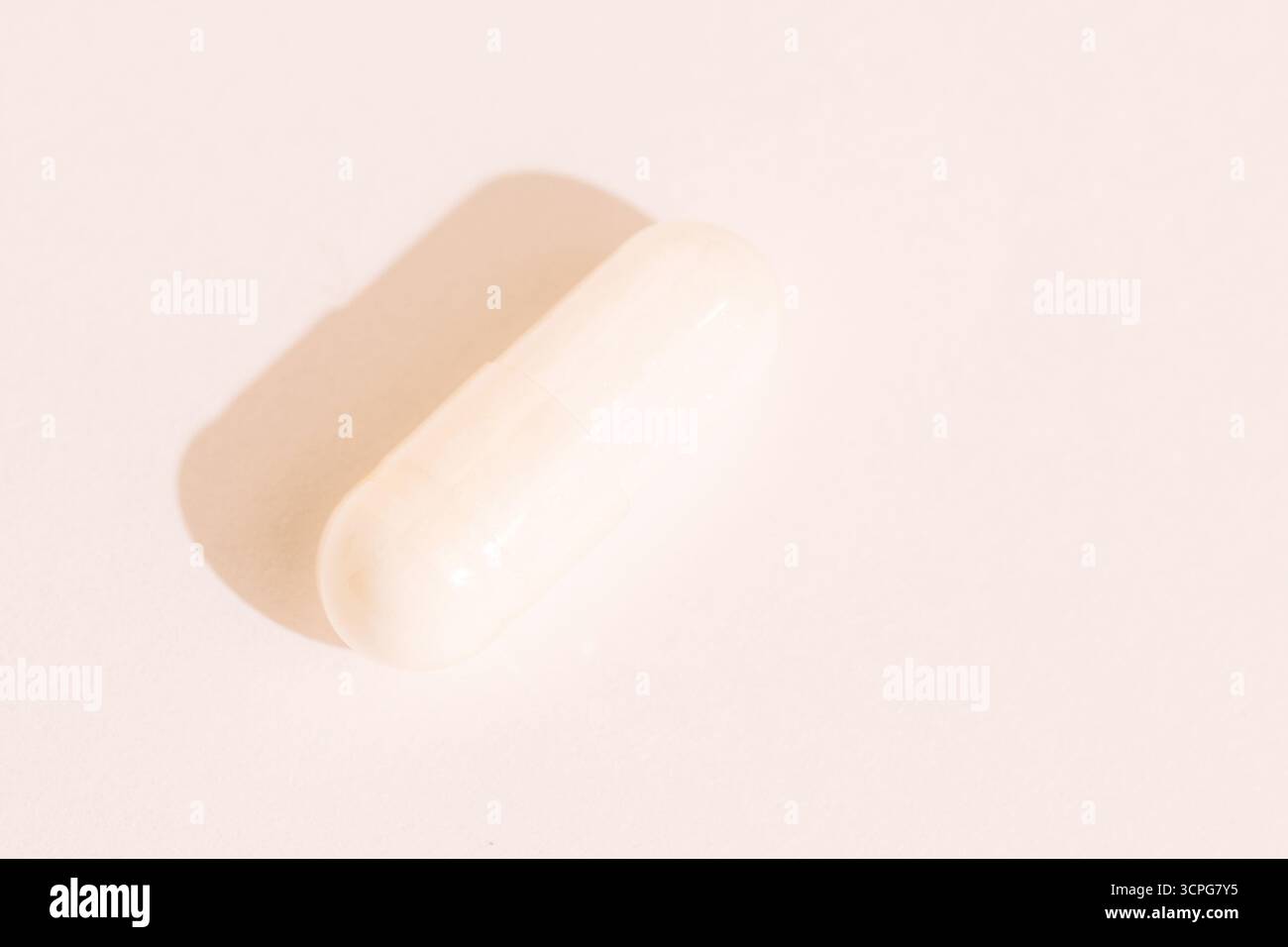 White dietary capsule close up lying with long shadow on soft pastel ...
