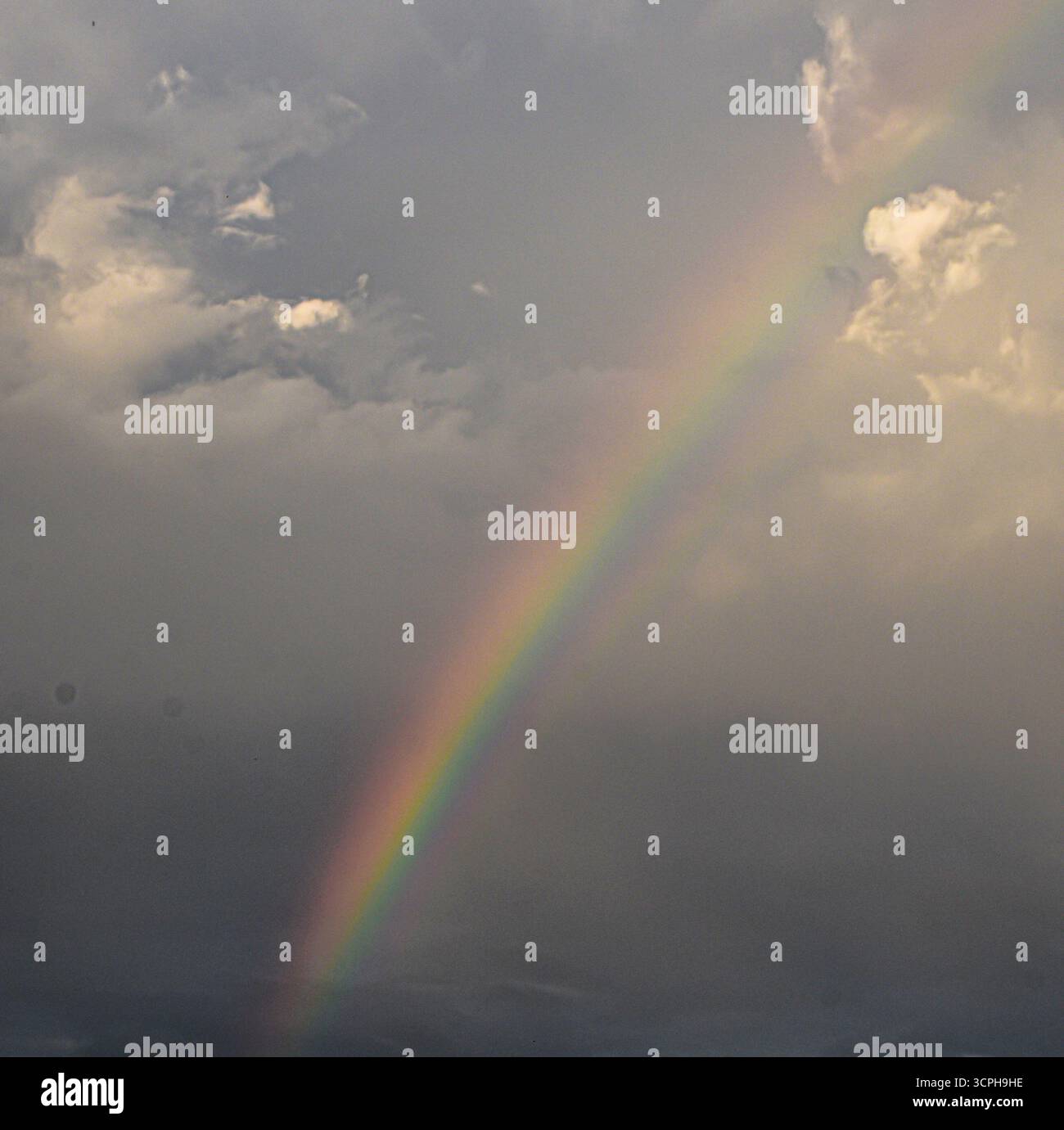 Beautiful rainbow stretches across a deep gray sky, casting vibrant ...