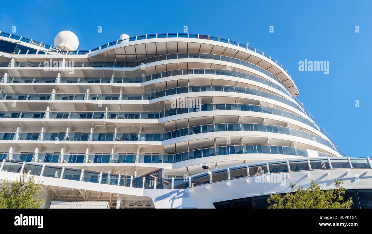 A large cruise ship with a sleek, modern design is docked at the harbor ...