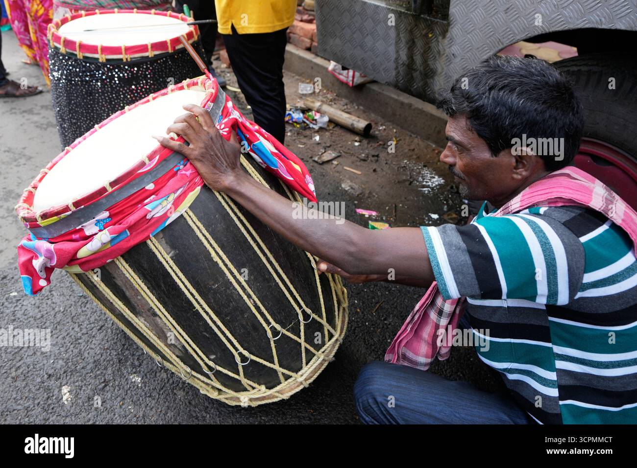 A traditional drummer tune his drum as he waits for customers to be ...