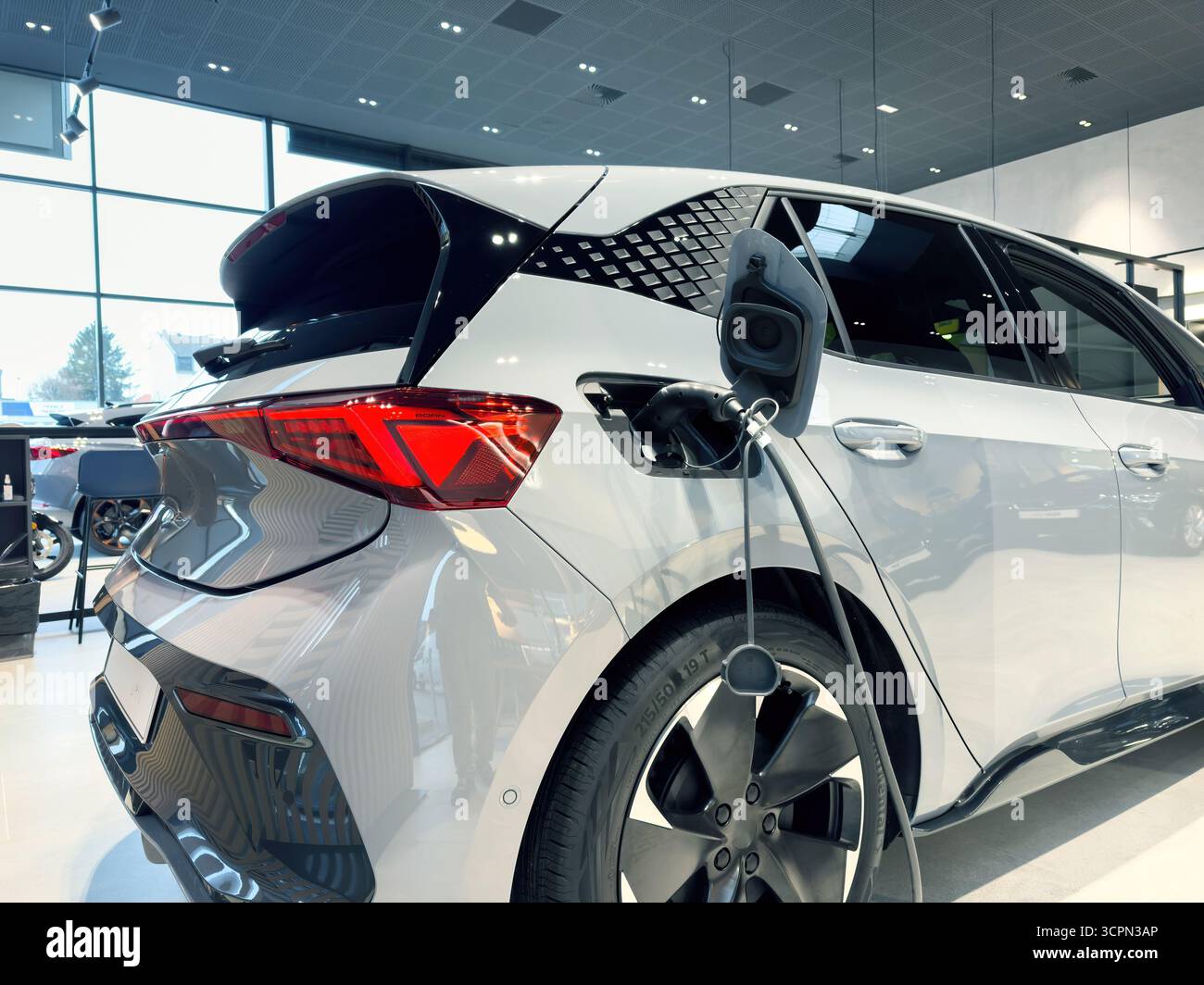 A sleek white electric hatchback car connected to a charging station ...
