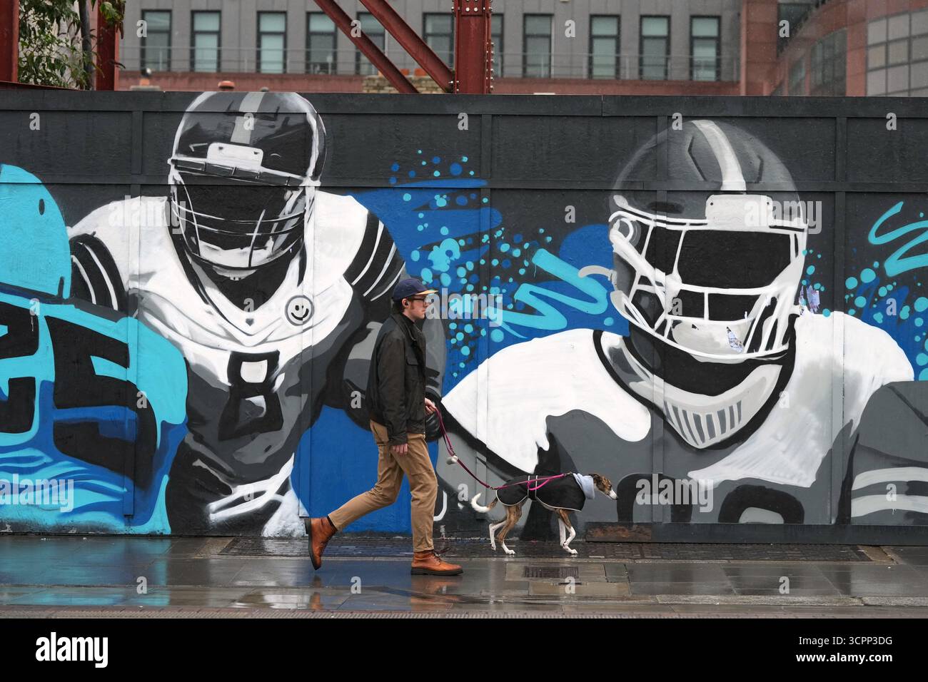 A m,an walks his dog past a temporary NFL football mural ahead of the ...