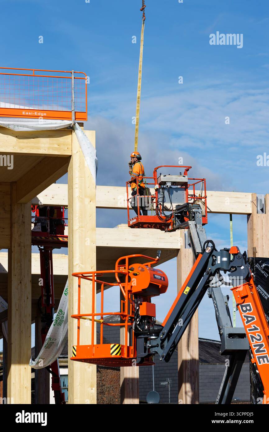 Laminated timber beam suspended from crane guided onto Glulam frame by ...
