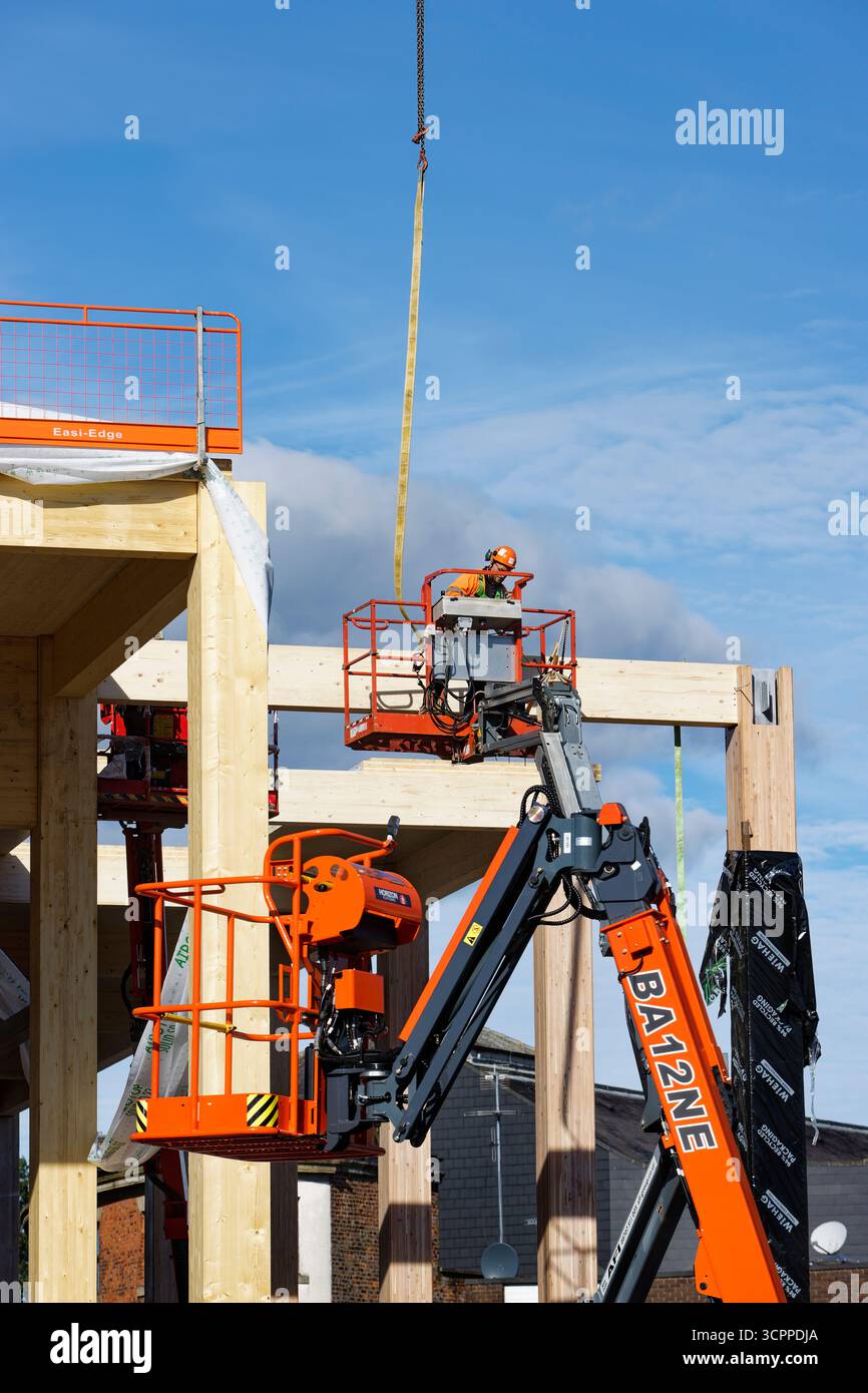 Laminated timber beam suspended from crane guided onto Glulam frame by ...