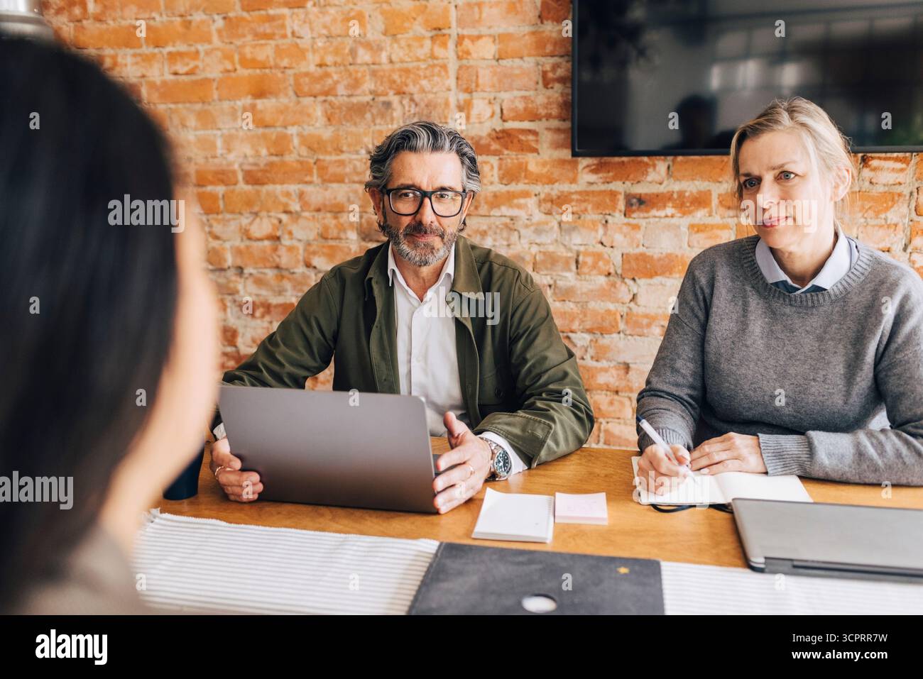 Senior businesswoman writing notes while sitting near male colleague ...