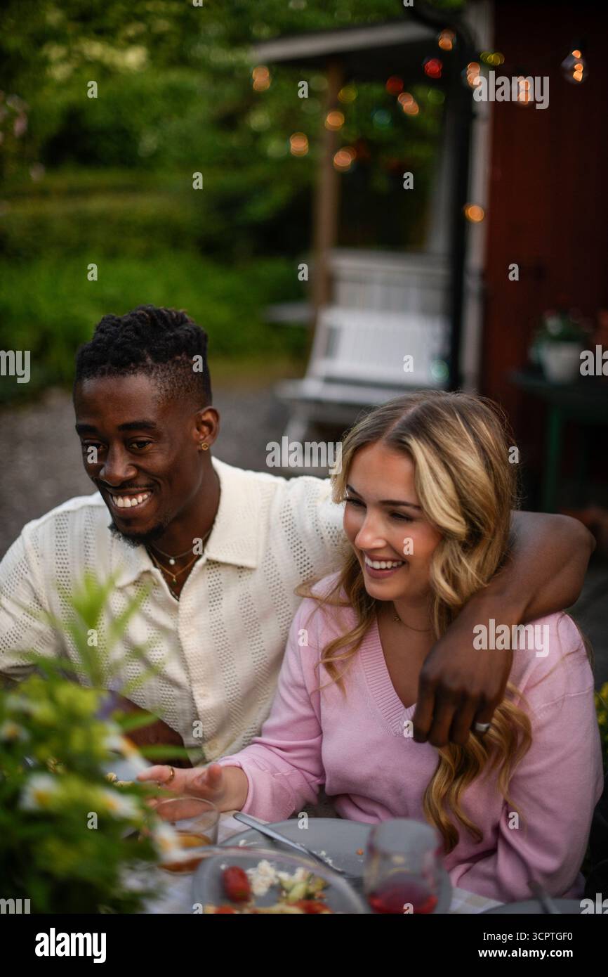 Smiling man sitting with arm around female friend at dinner party in ...