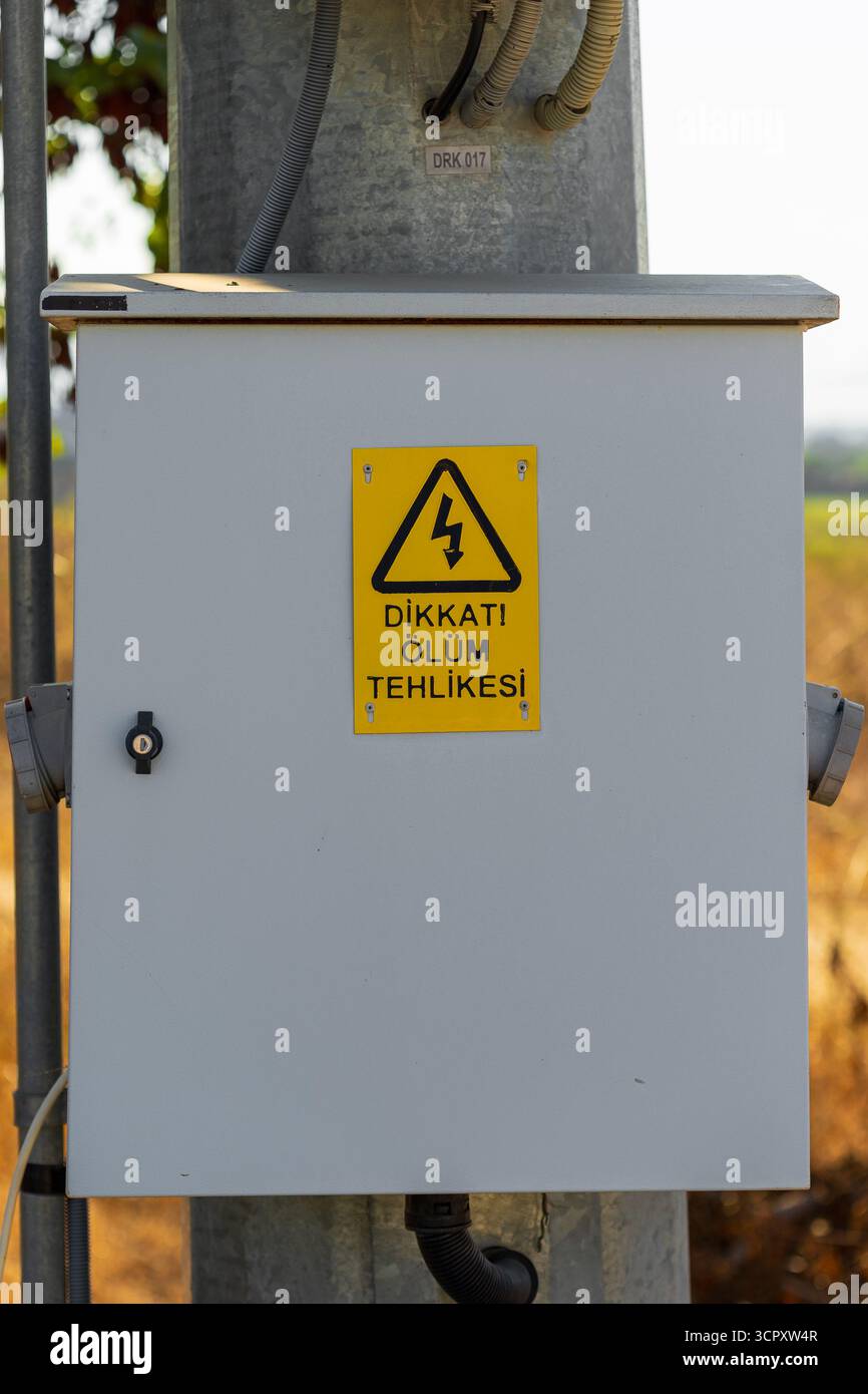 A gray electrical box mounted on a metal pole, featuring a yellow ...