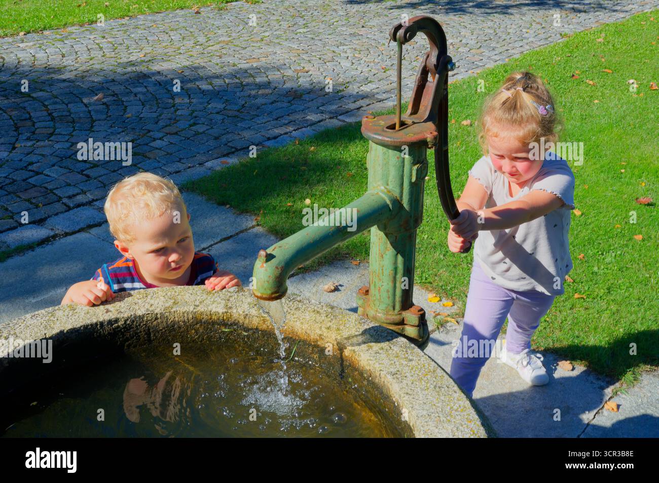 Wasserspiele. Kinder spielen am Brunnen mit der alten Wasserpumpe ...