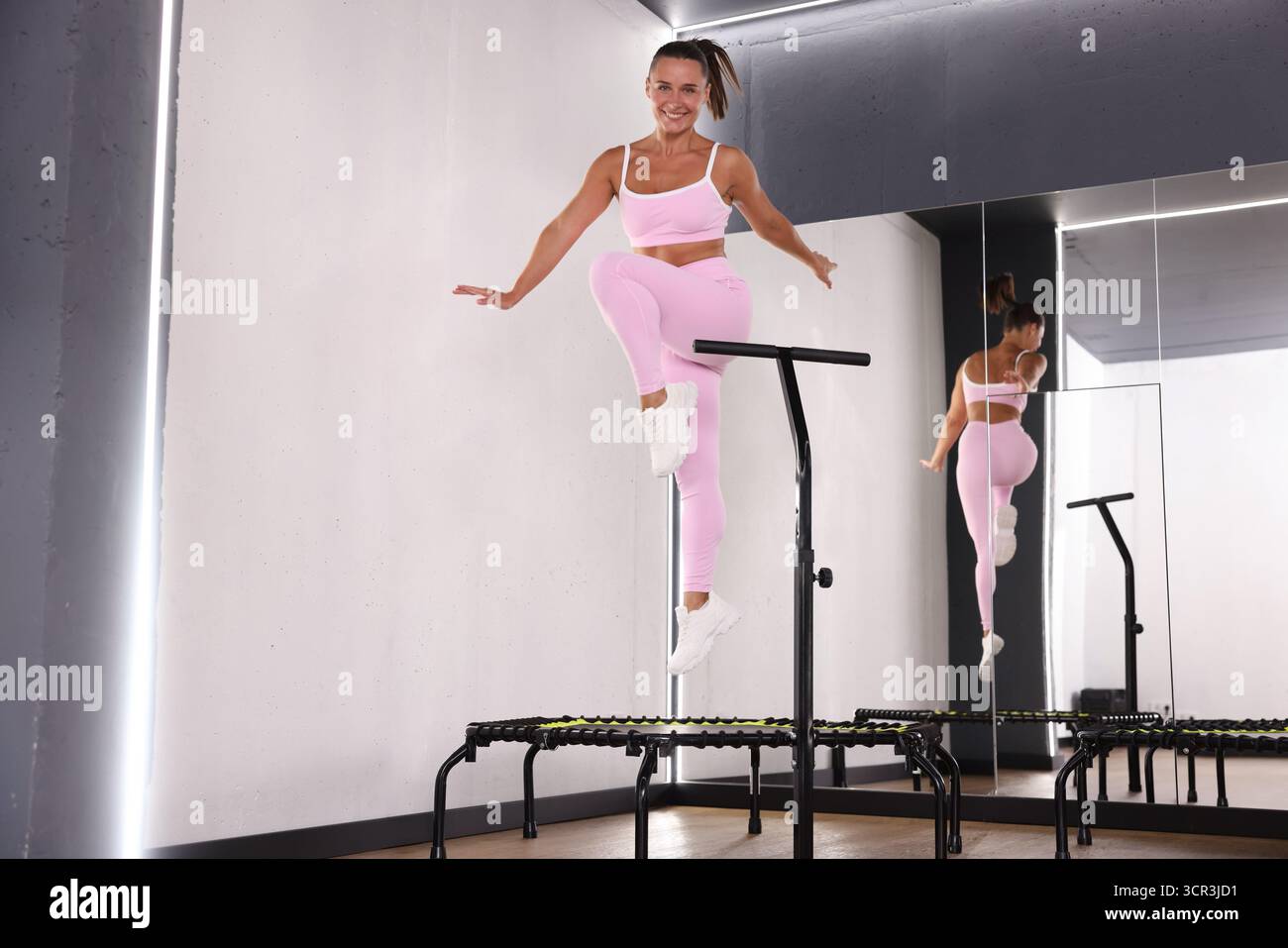 Smiling woman jumping on mini exercise trampoline near mirror in ...