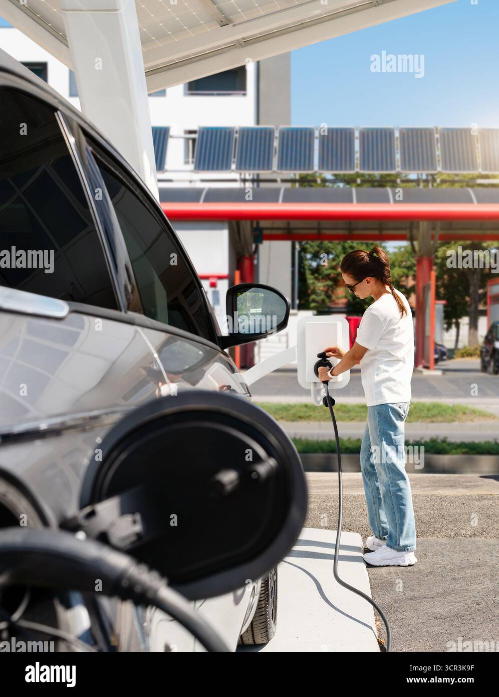 Female driver charging electric car on EV station with solar panels in ...