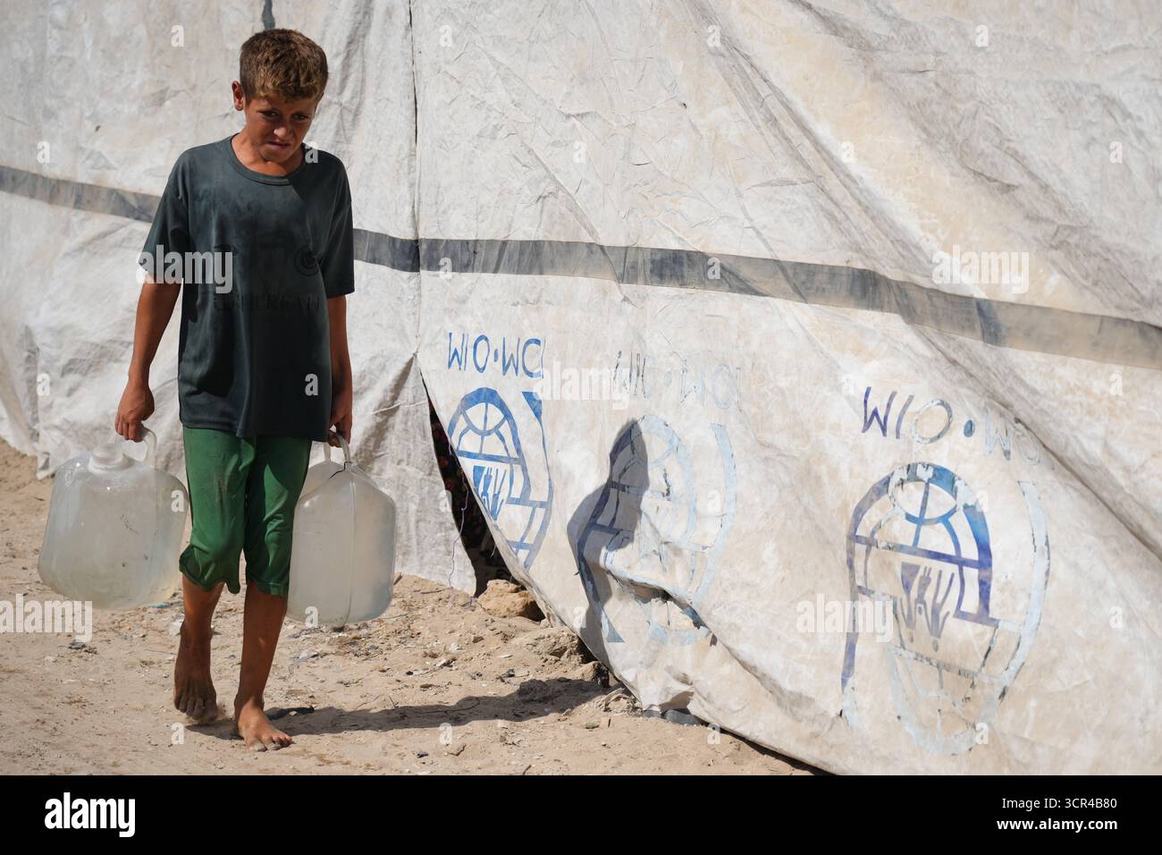 A displaced Palestinian child carries jerrycans after collecting water ...
