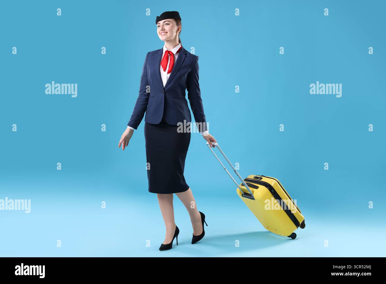 Positive stewardess with suitcase on light blue background Stock Photo ...