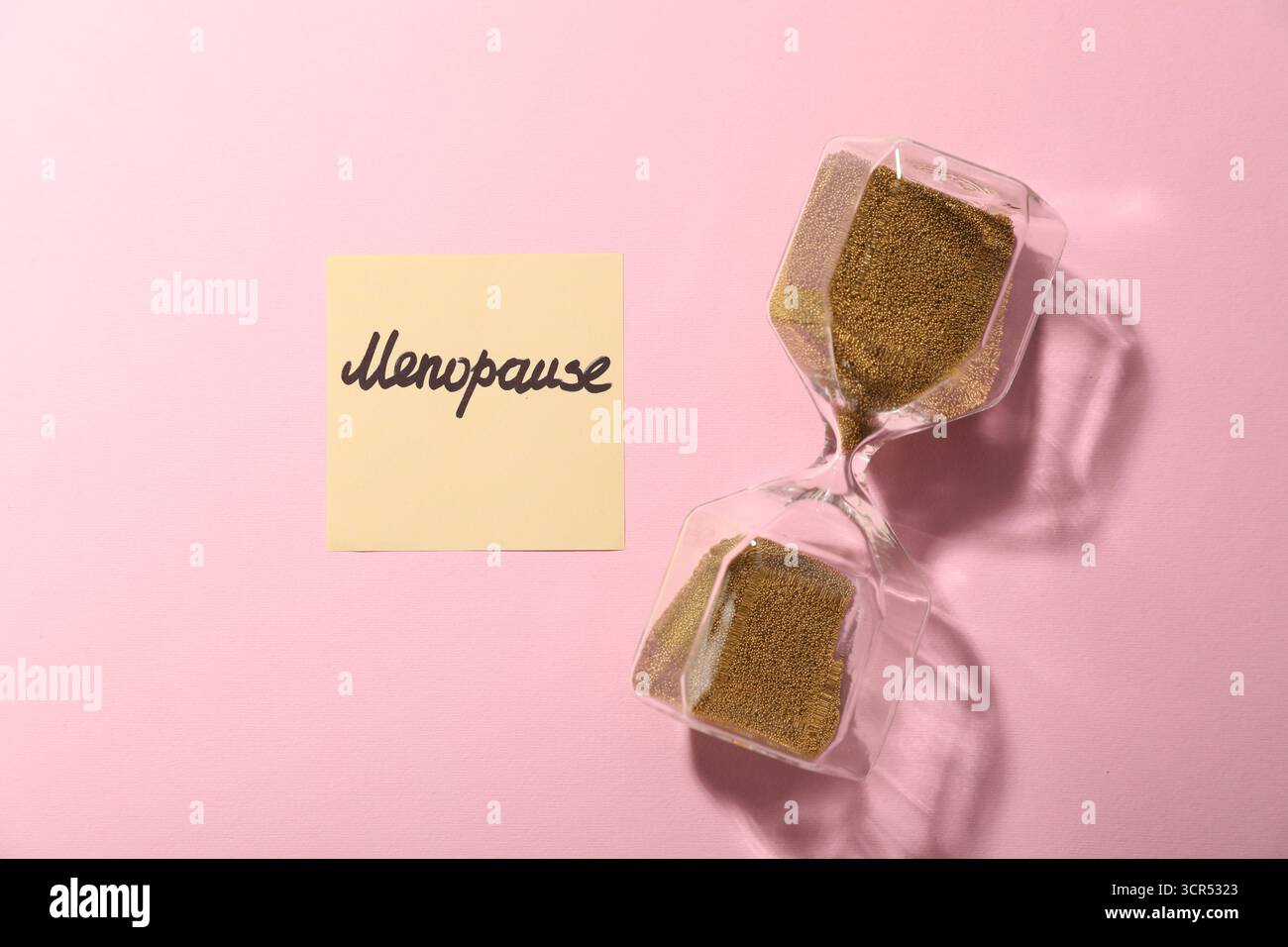 Paper note with word Menopause and hourglass on pink background, top ...