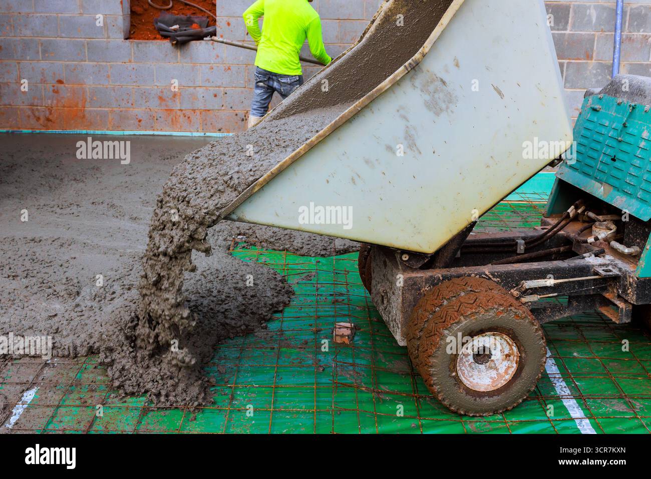 Wet concrete is being poured from dumping wheeled concrete wheelbarrow ...