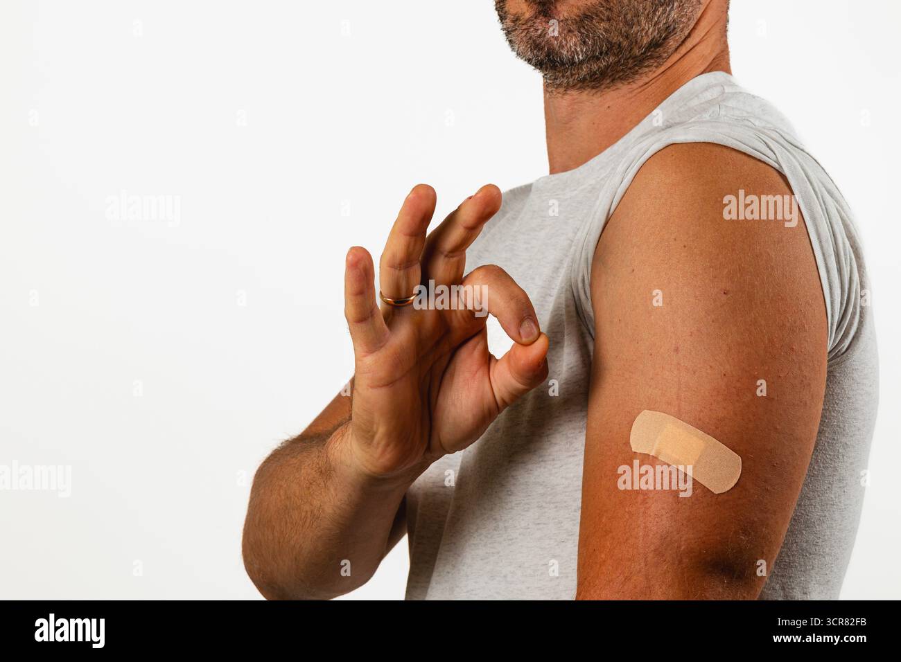 A man stands with a bandage on his upper arm, smiling and gesturing an ...