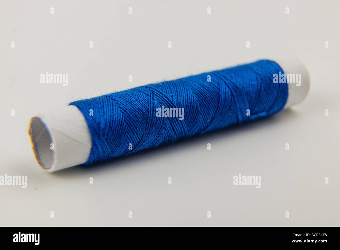A vibrant blue spool of sewing thread rests flat, showcasing its smooth ...