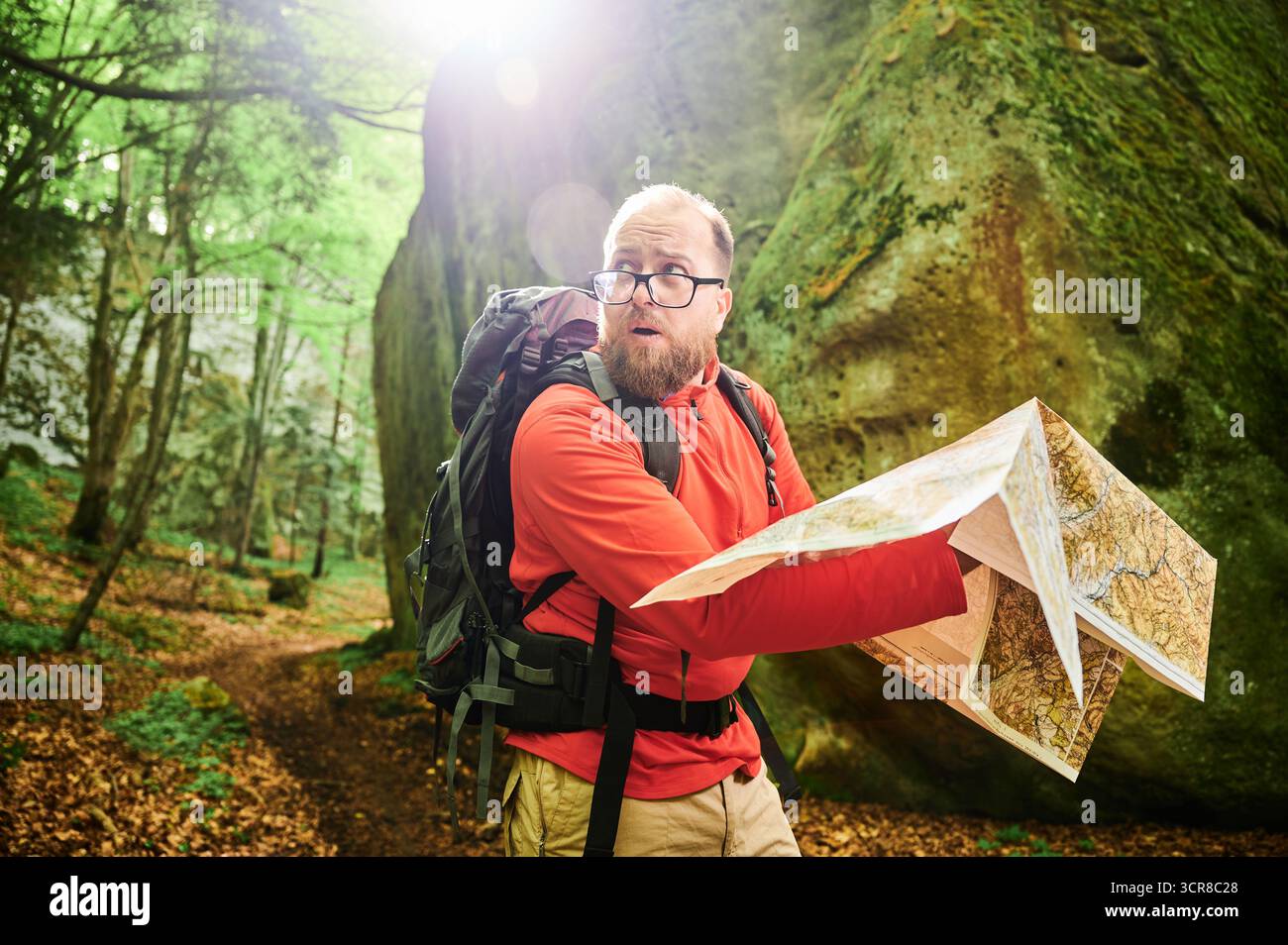 Bearded tourist man looks puzzled, studies map while stands in front of ...