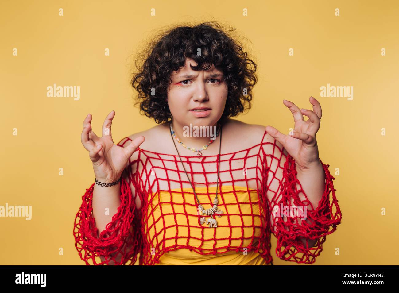 Woman wearing a red netted top against a yellow background shows an ...