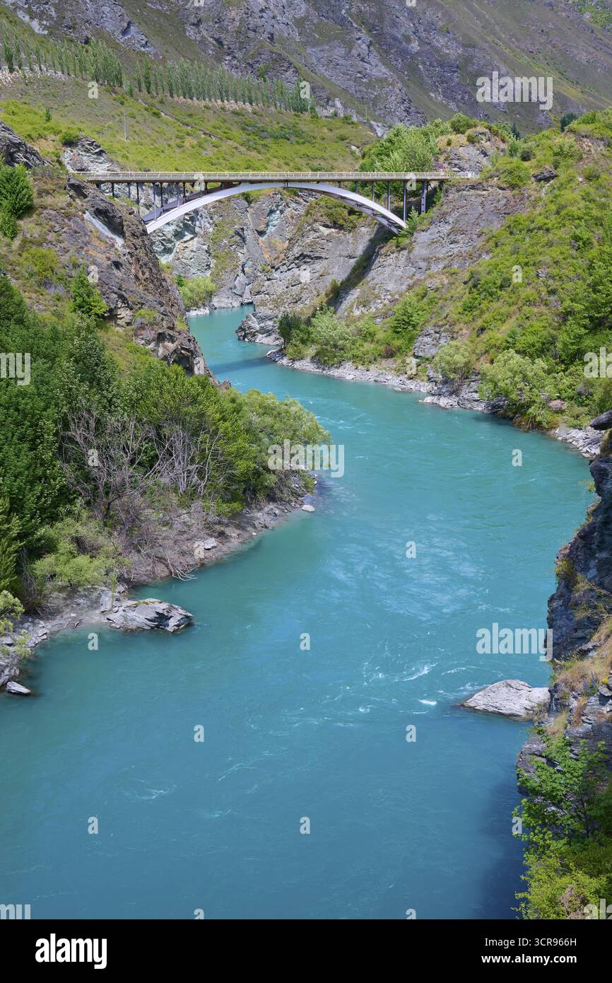 A turquoise-coloured river flows through a green valley with a bridge ...