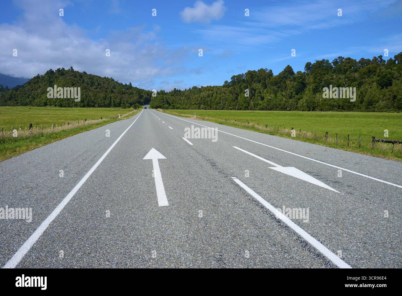 Wide road with arrows leads through green landscape under blue sky ...