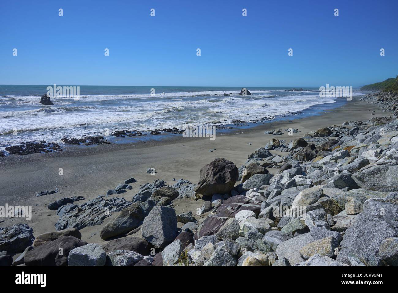 Rocks spread along a sunny sandy beach with waves in the background ...