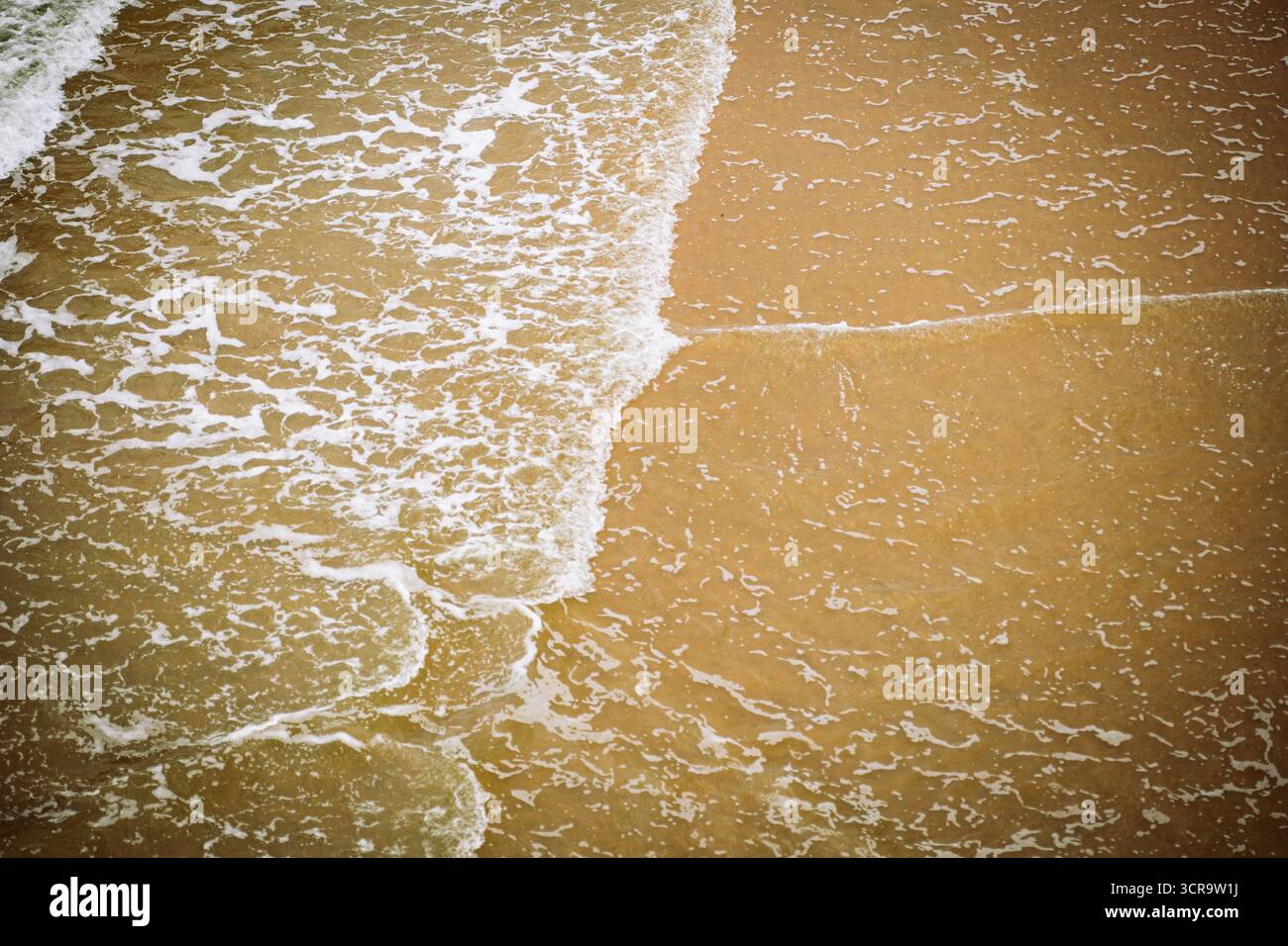 Foamy, shallow, tidal waves reaching the sandy shore. Top down view ...