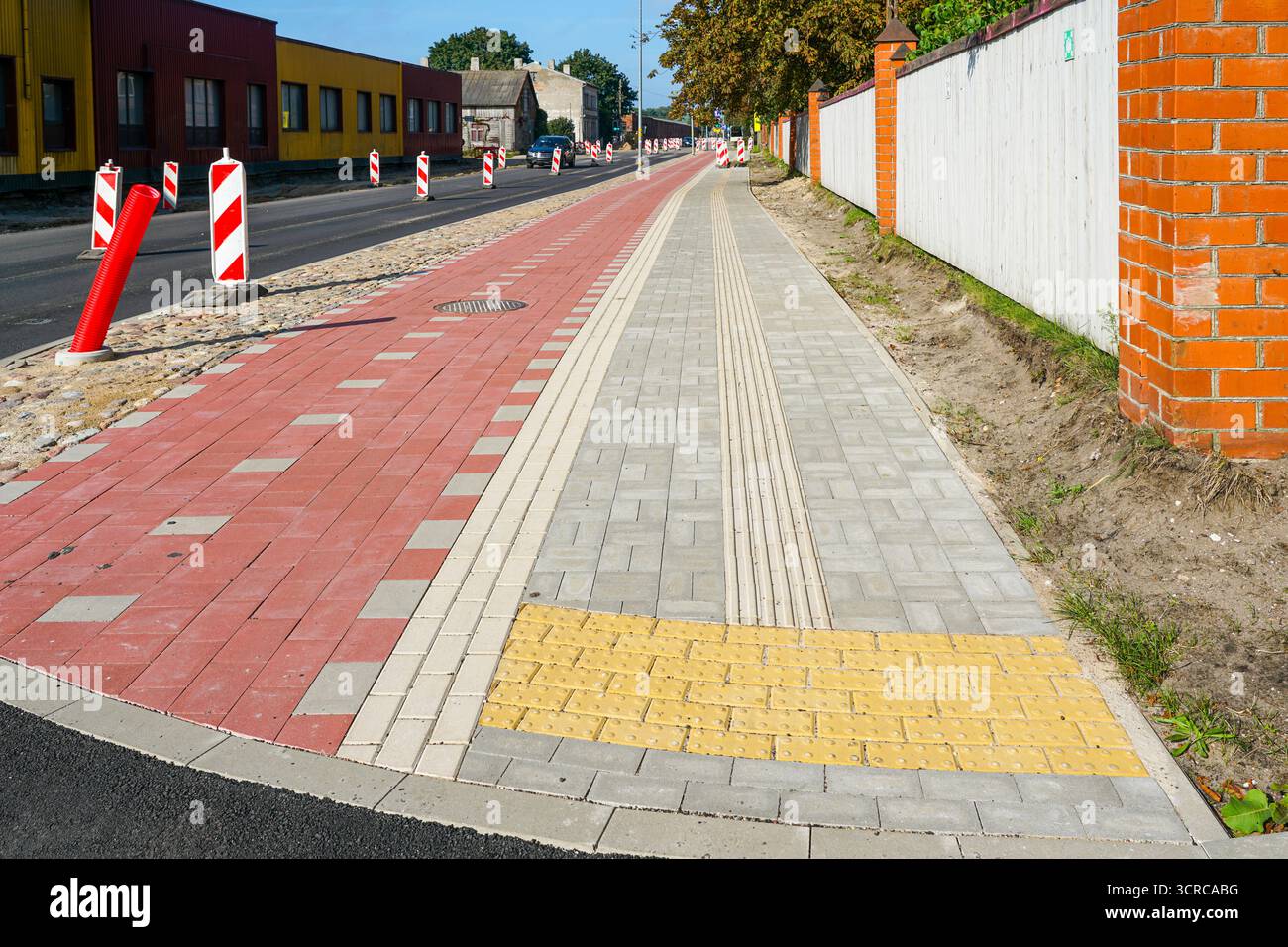 Modern city sidewalk with red, gray, and yellow paving blocks, tactile guidance strips, and ...