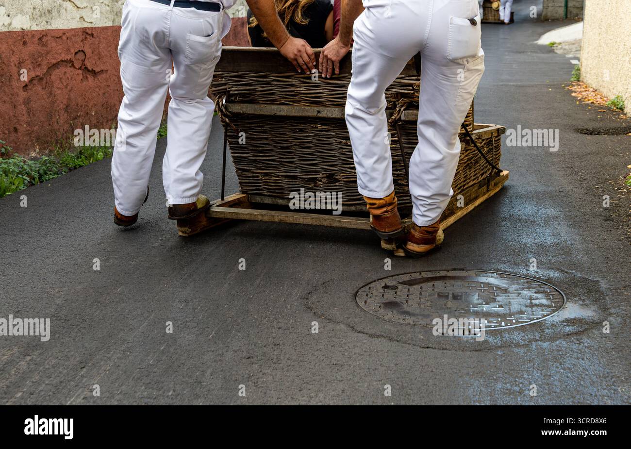 Two men in white uniforms push a traditional wicker basket toboggan ...