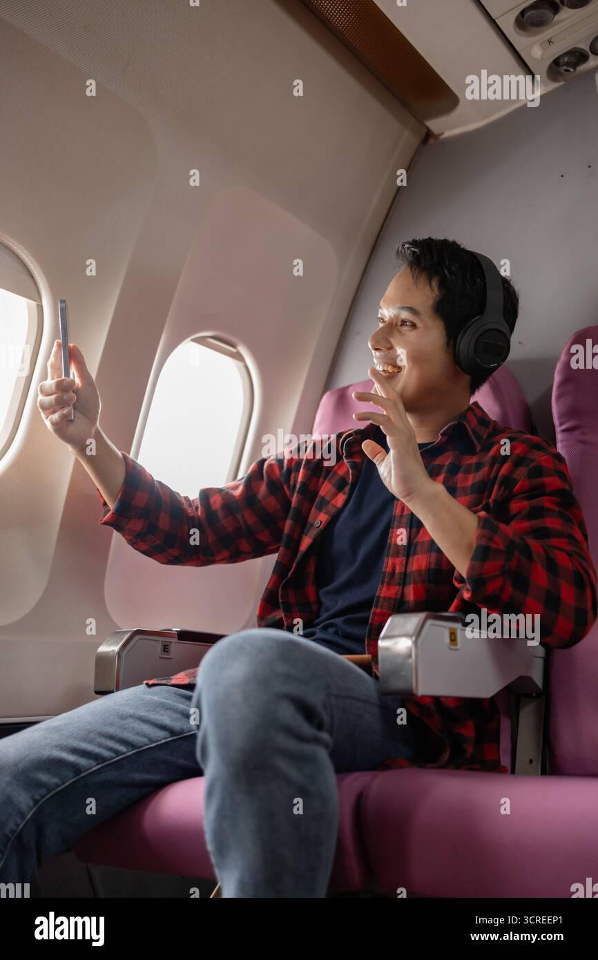 Young Asian man sitting on airplane seat taking a selfie with his ...
