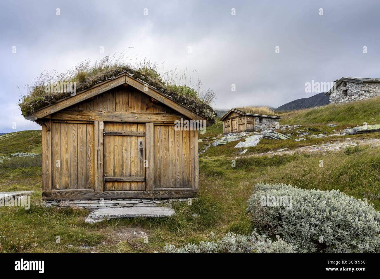 Wooden huts with grass-covered roofs in a hilly, rural landscape under ...