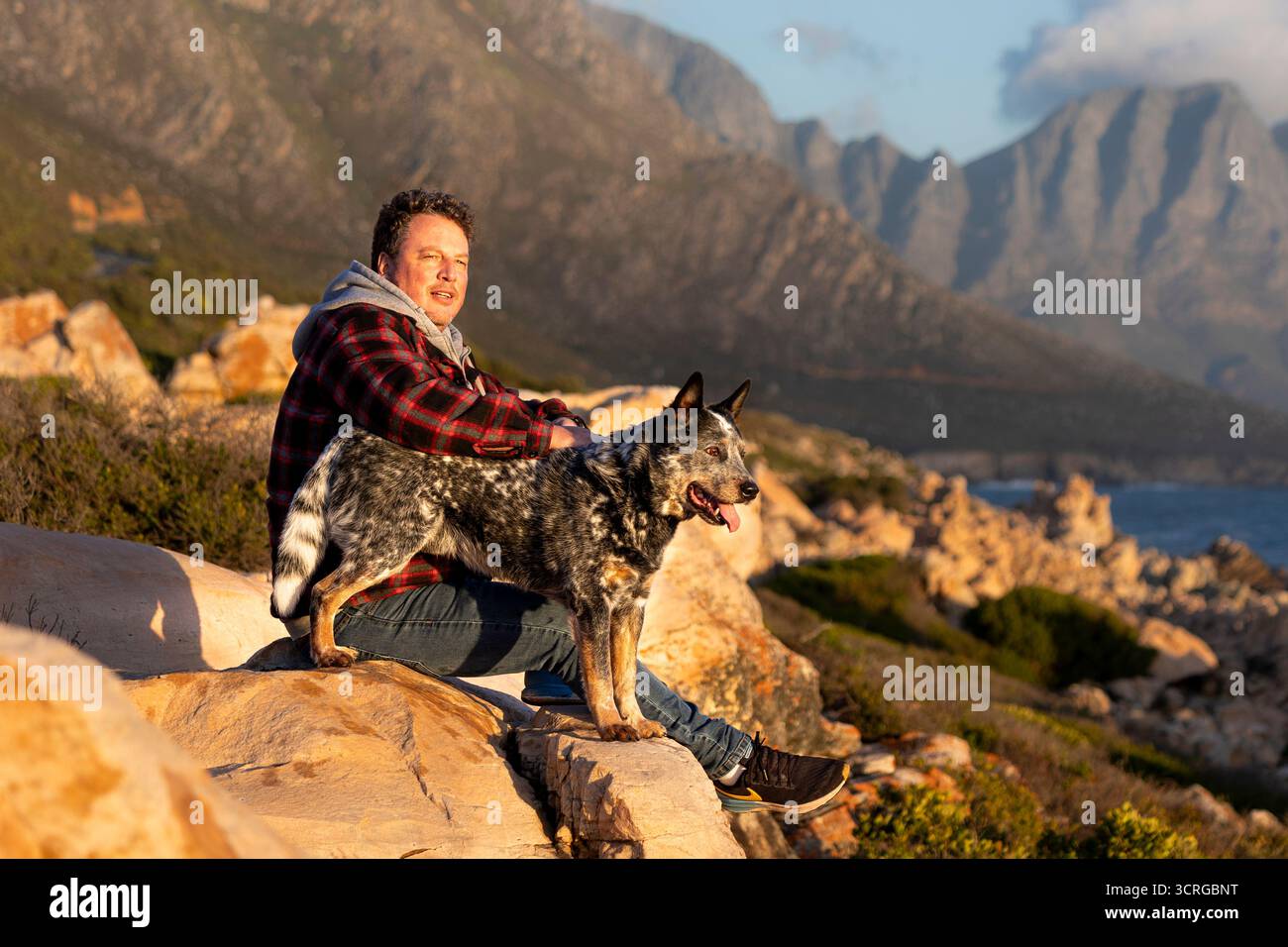 Man sitting outdoors with his arm resting on his Australian Cattle dog ...