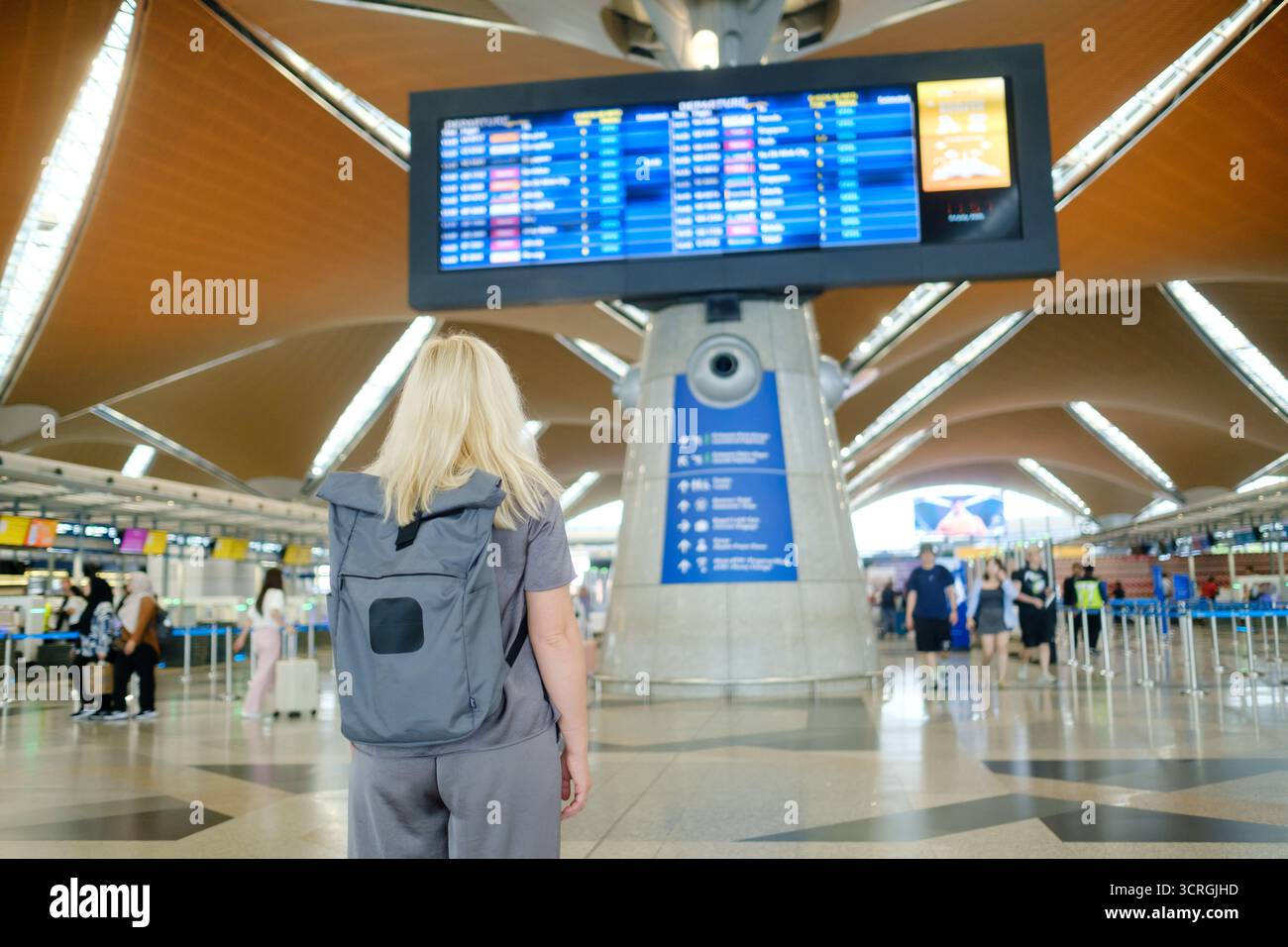 A traveler stands in an airport terminal, facing a digital flight ...