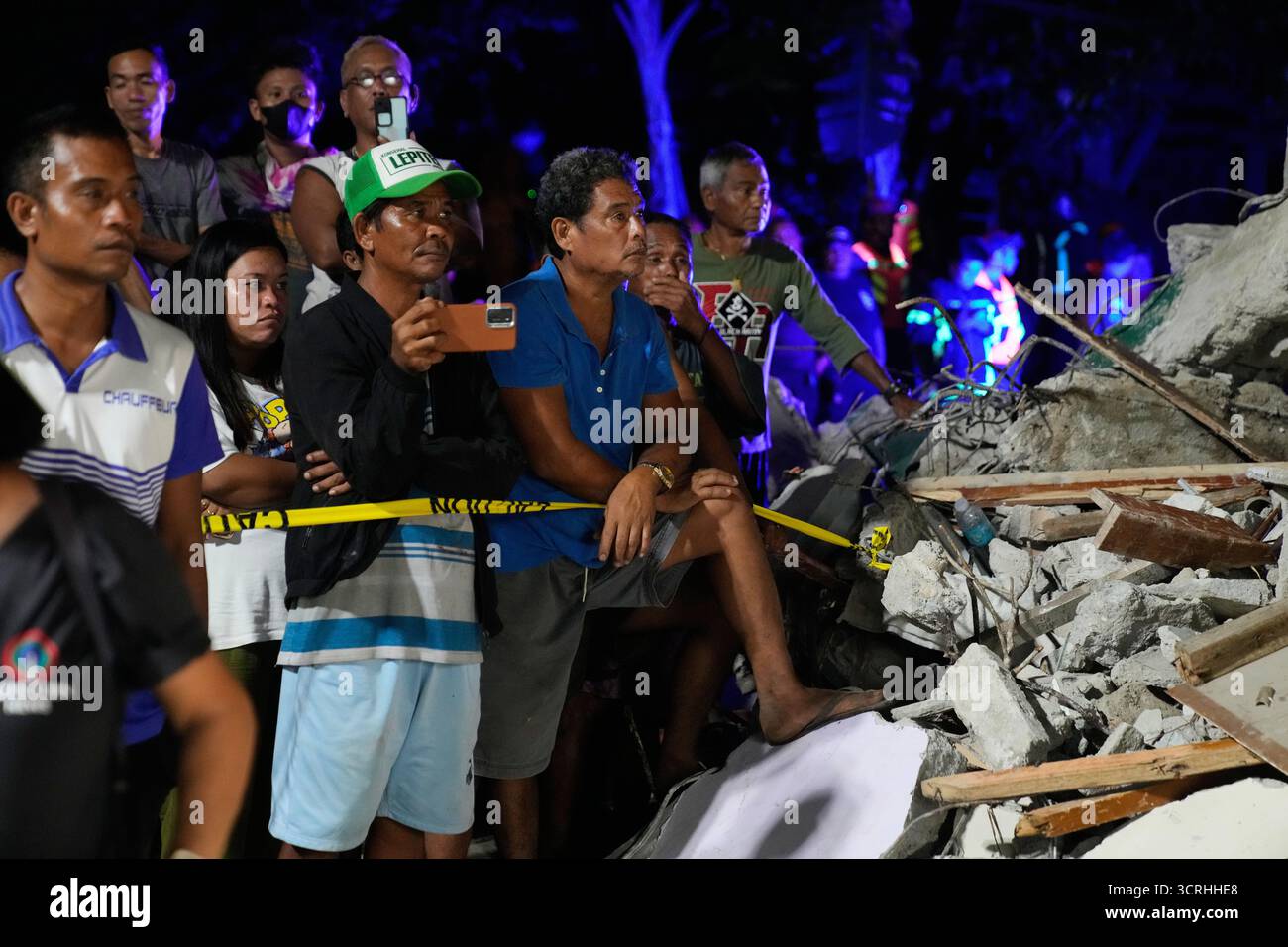 Residents look as rescuers search for survivors at a collapsed building ...