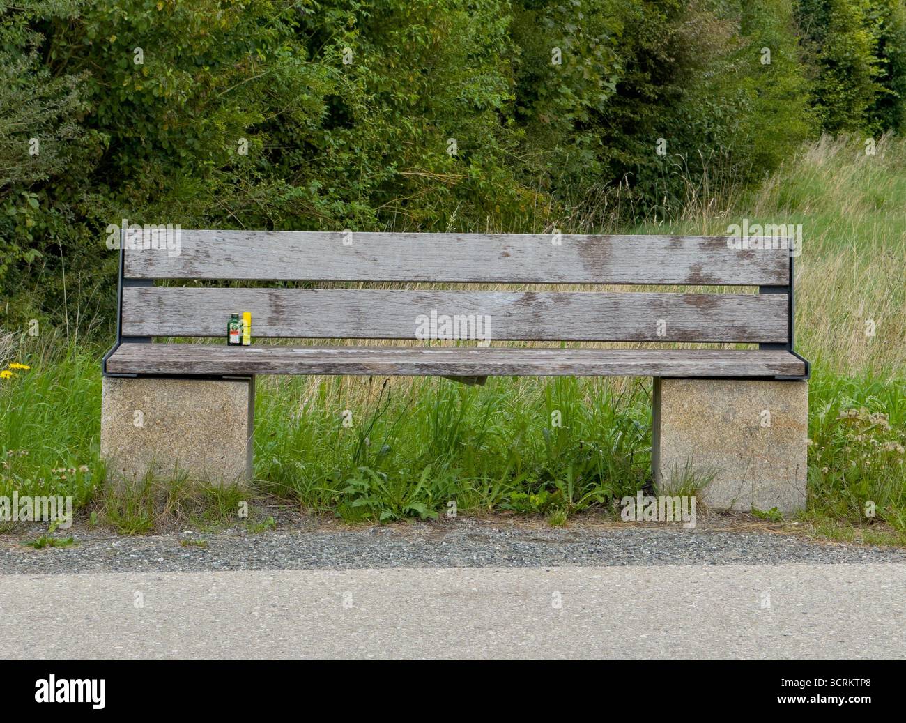 Two small bottles sit on a sunlit, worn wooden bench in a grassy ...