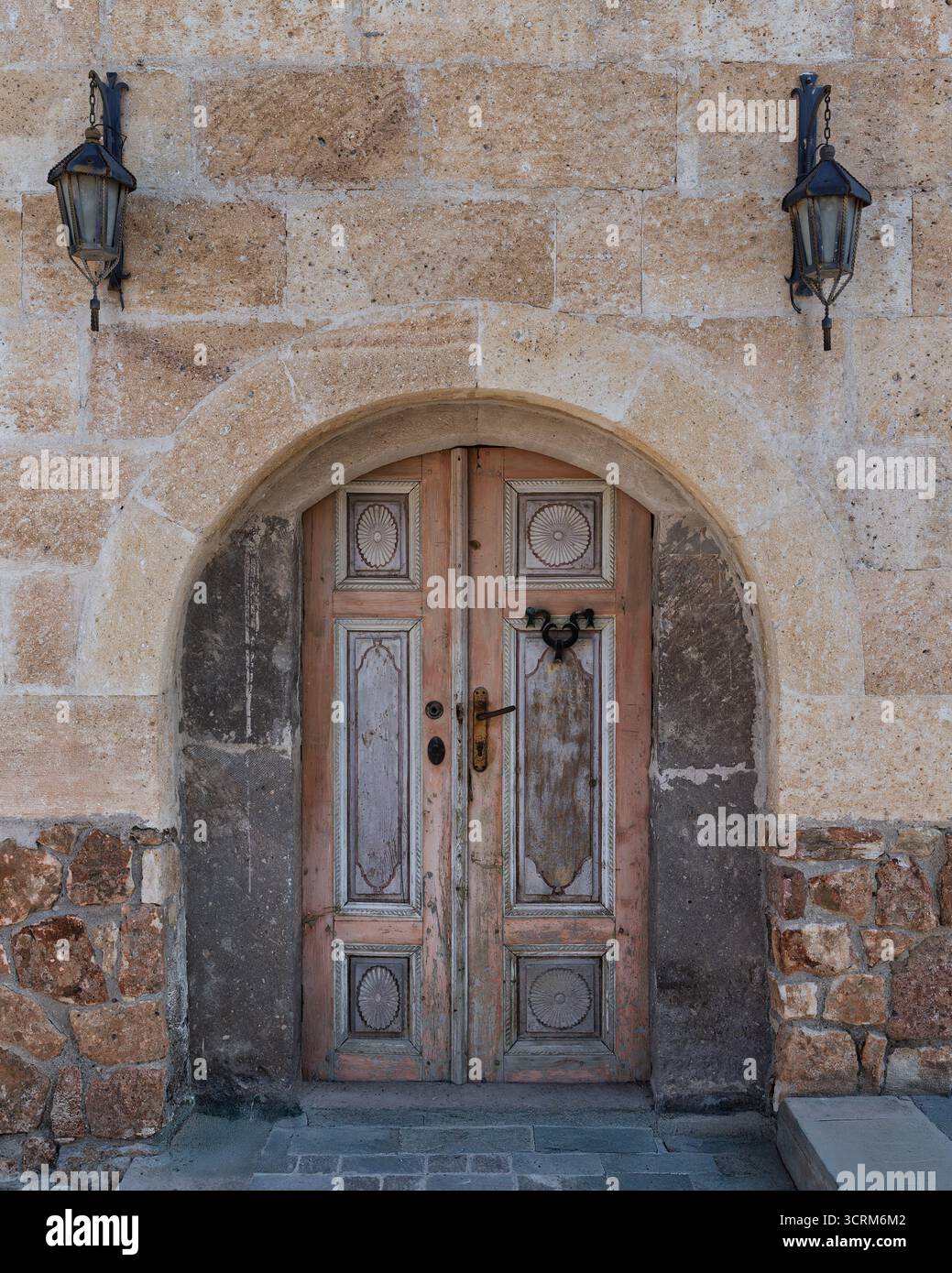 Rustic arched stone doorway with a weathered wooden door, peeling pink ...