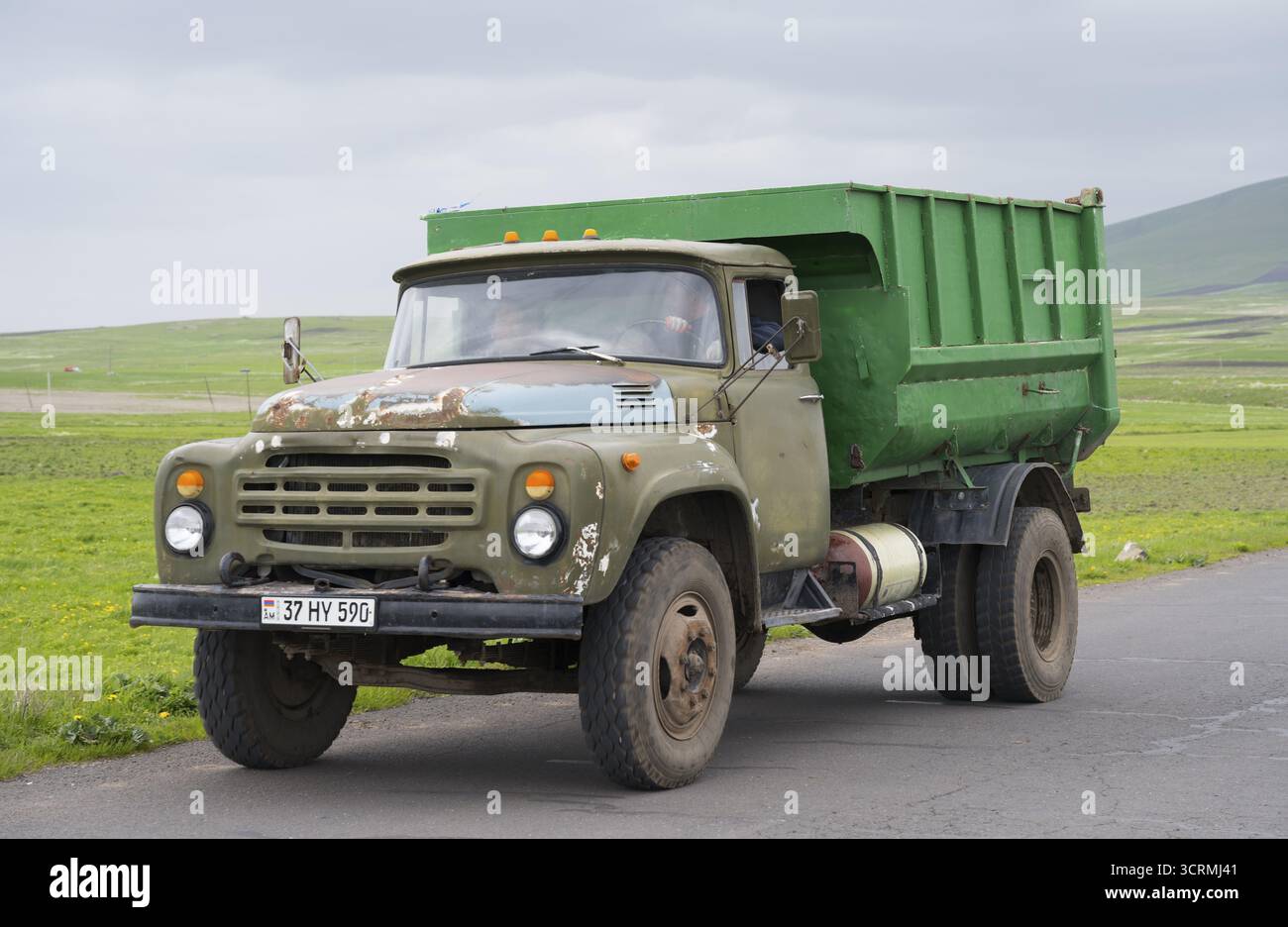 A green lorry with visible signs of wear driving on a country road in ...