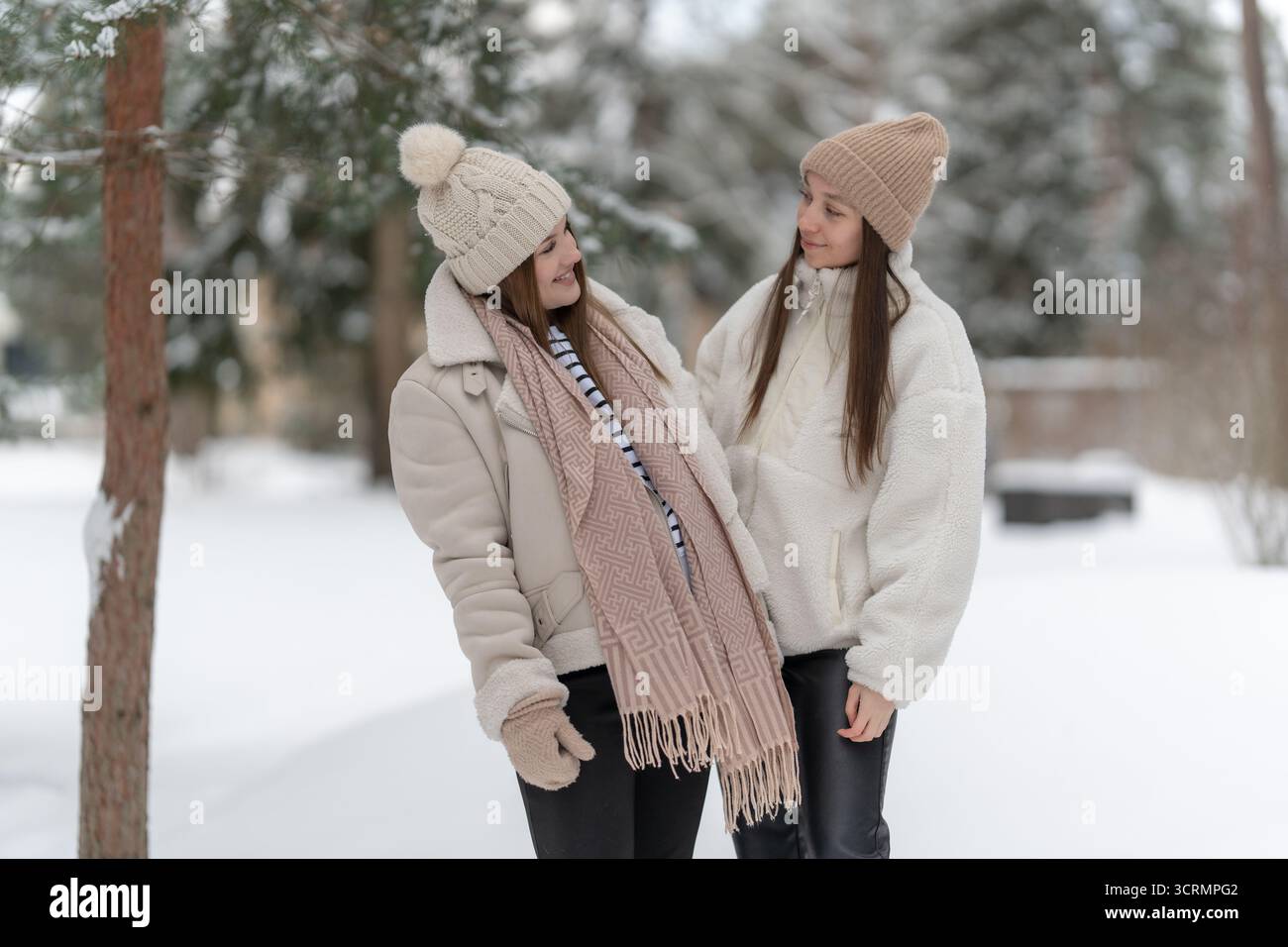 Two young women friends talking and laughing in a snowy park, dressed ...