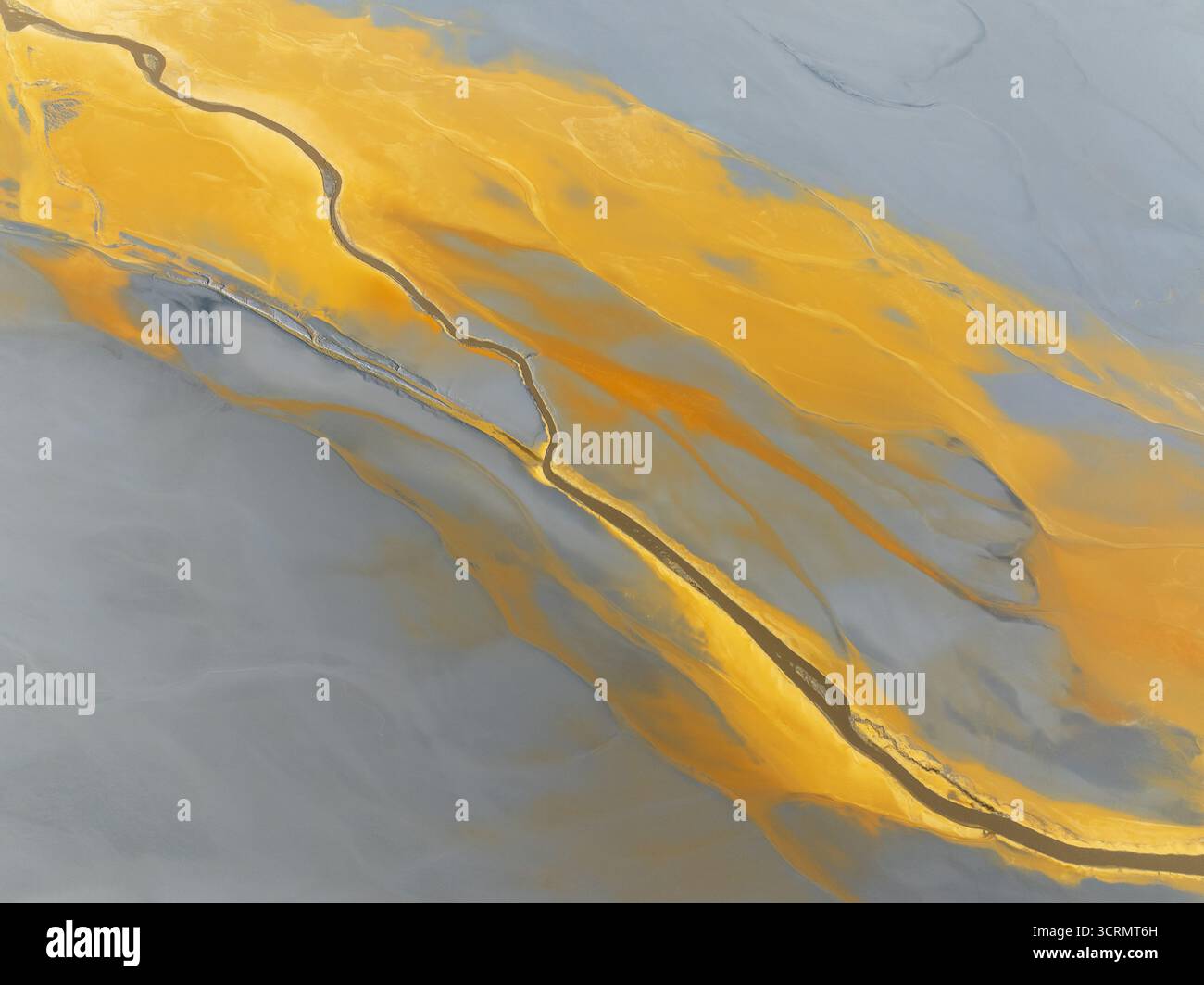 Aerial view of a vibrant golden stream snaking through the stark, grey ...